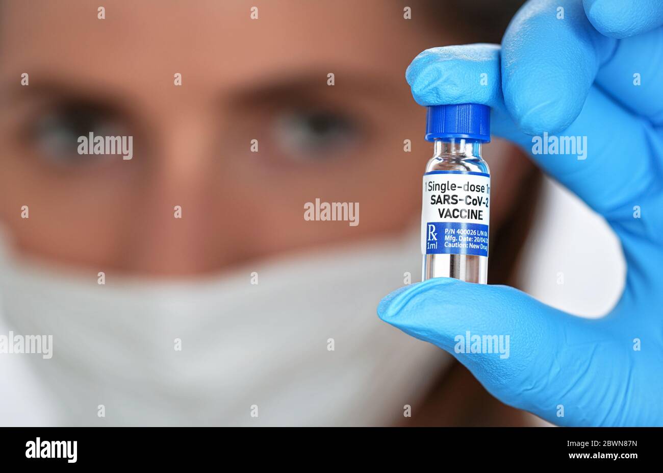 Hand in blue medical gloves holds small vial with label SARS-Cov-2 ...