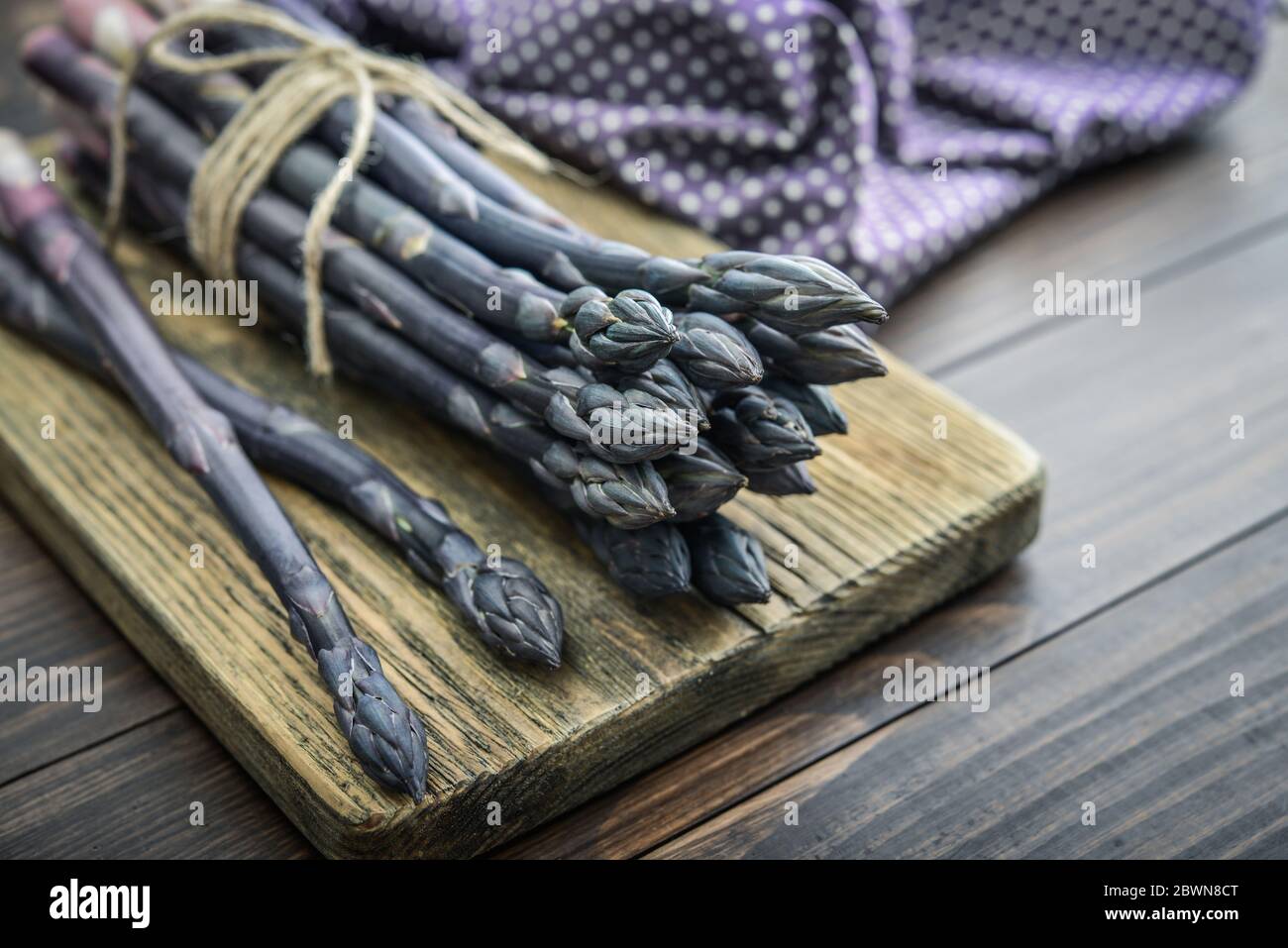 An edible, raw stems of asparagus on tray on a wooden background, top ...