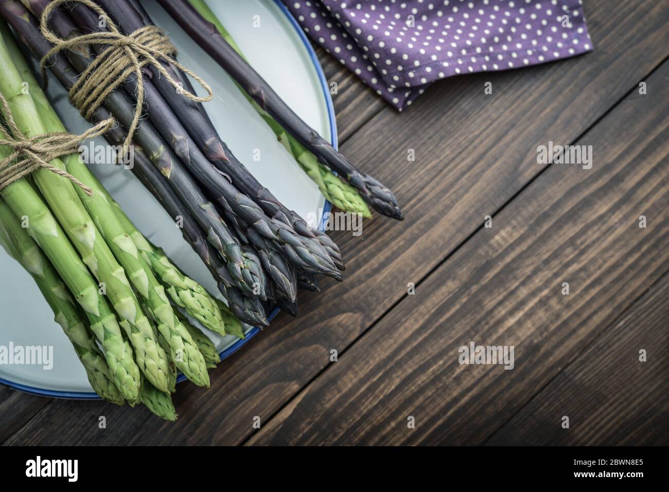 An edible, raw stems of asparagus on tray on a wooden background, top ...