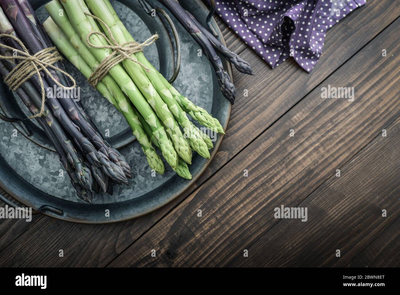 An edible, raw stems of asparagus on tray on a wooden background, top ...