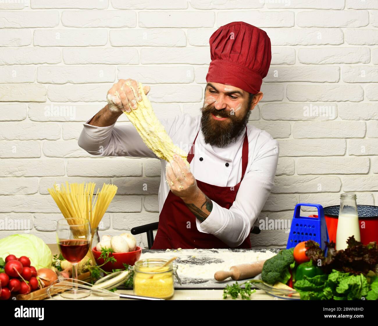 Chef makes dough. Man with beard stretches kneaded dough on white brick ...