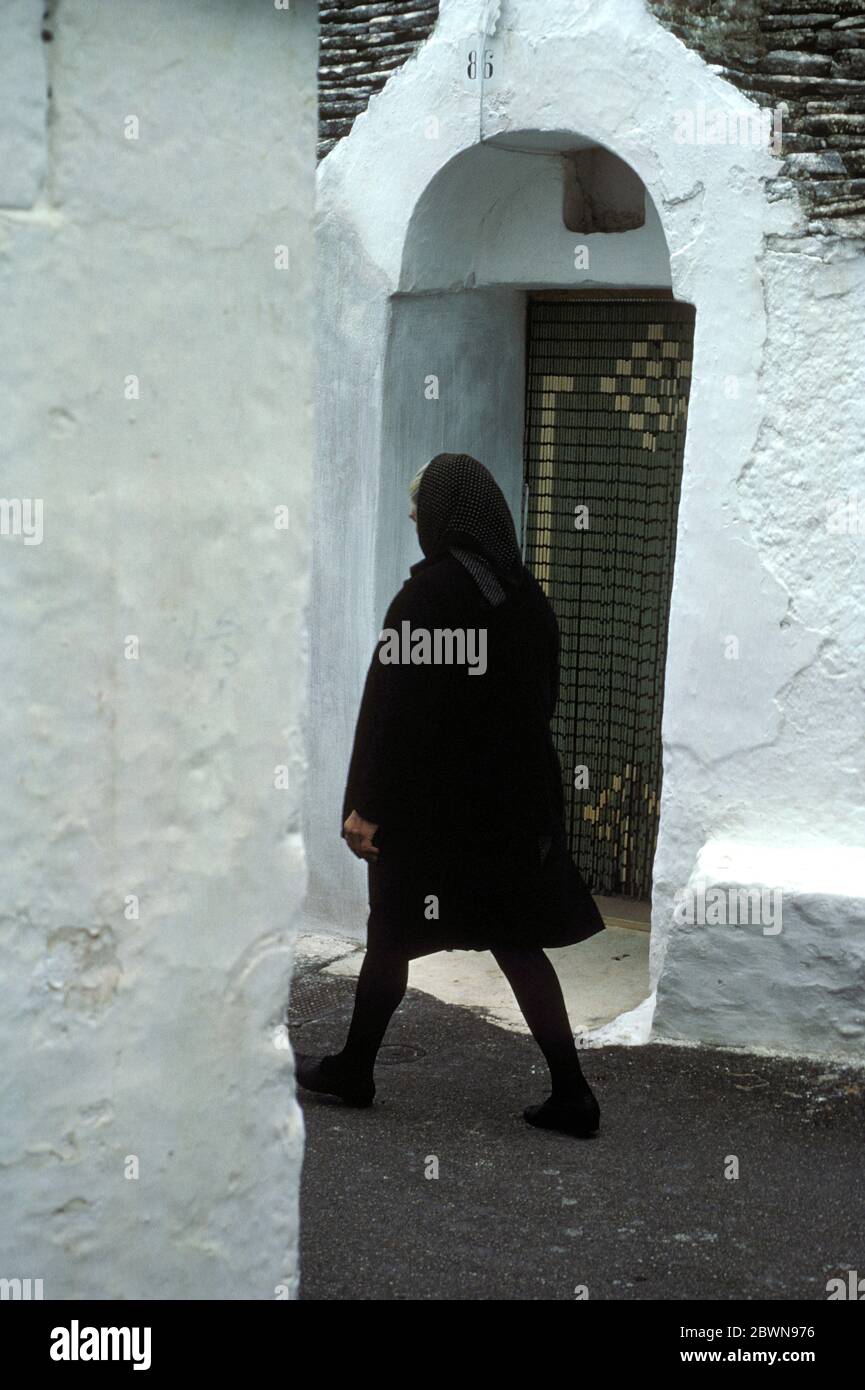 A widow walking through a street with Trulli houses in Alberobello in ...