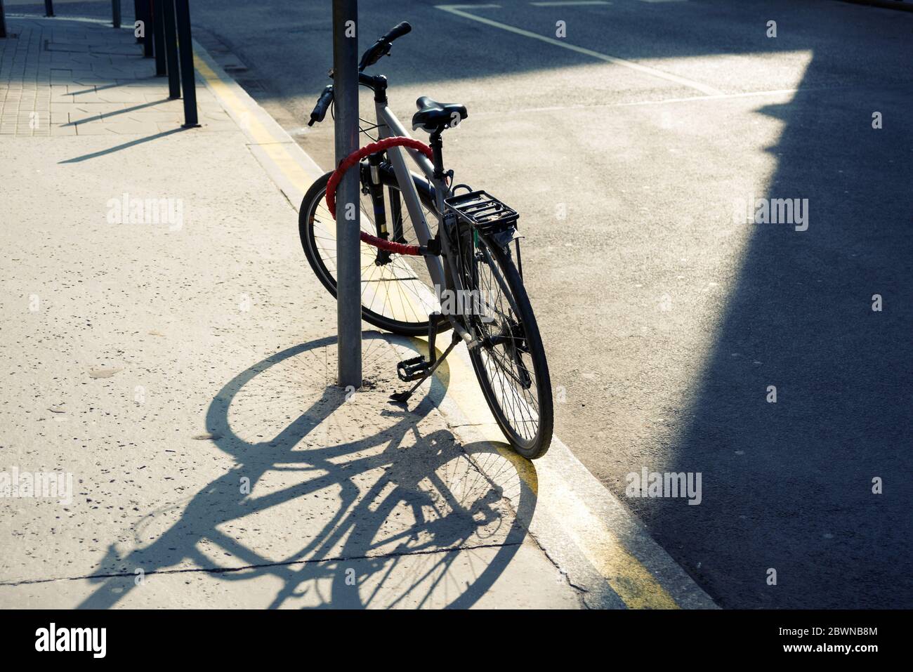 Sunlit sport bicycle leaned to post by the road Stock Photo - Alamy