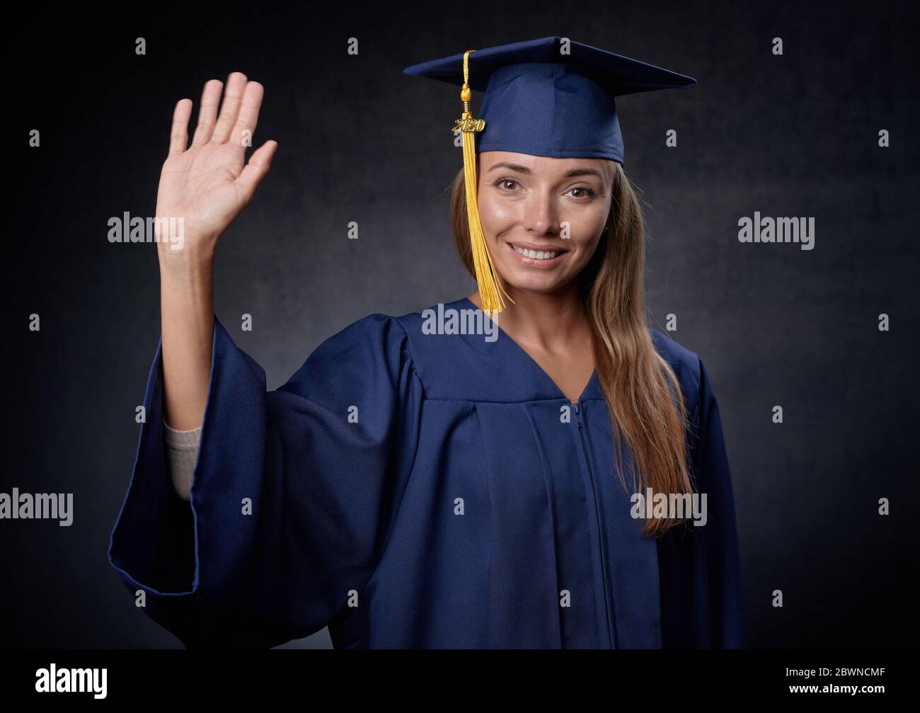 Smiling young woman waving hand wearing blue cap and gown Stock Photo ...