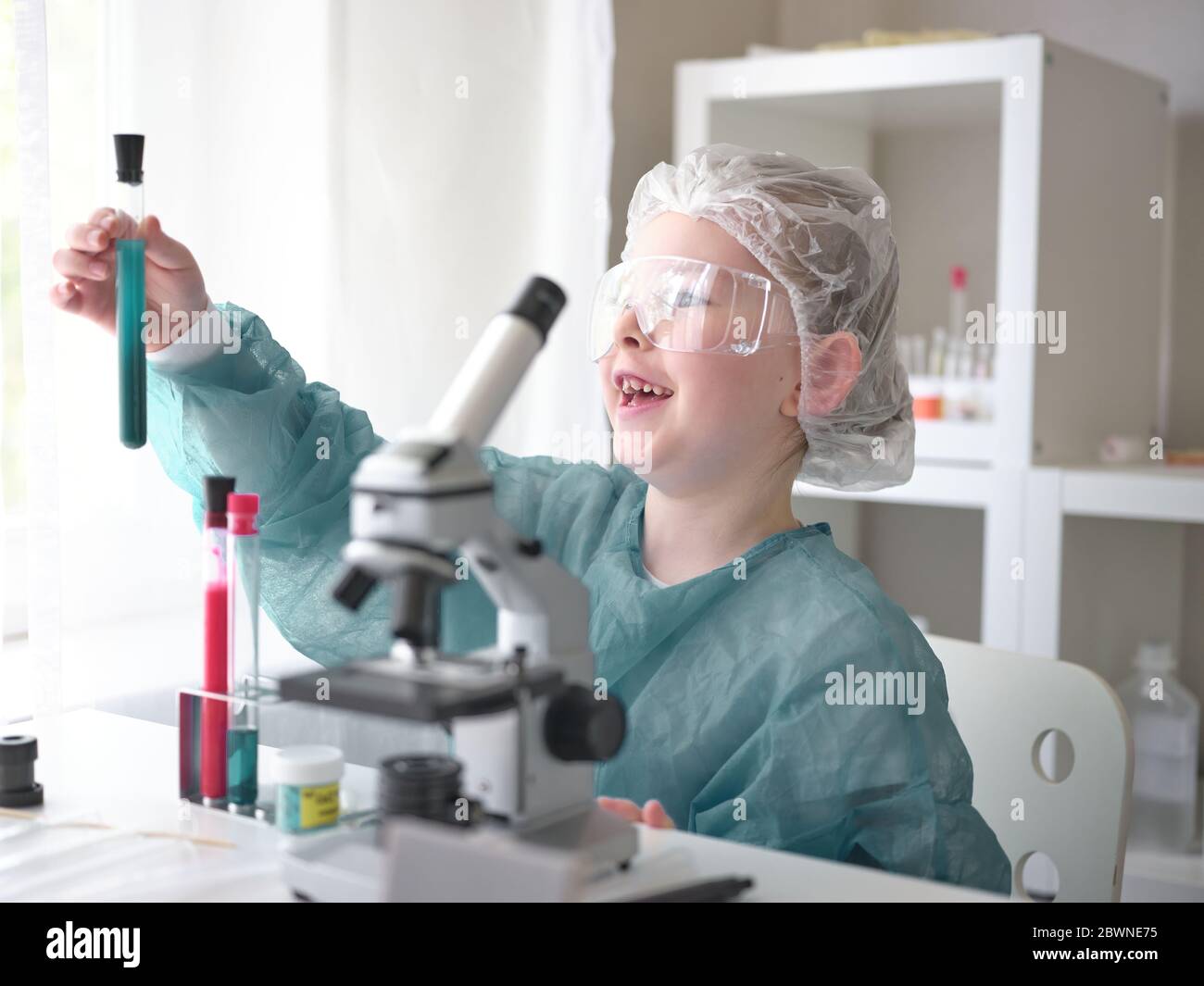 Cute little girl looking into microscope at his desk at home. Young ...
