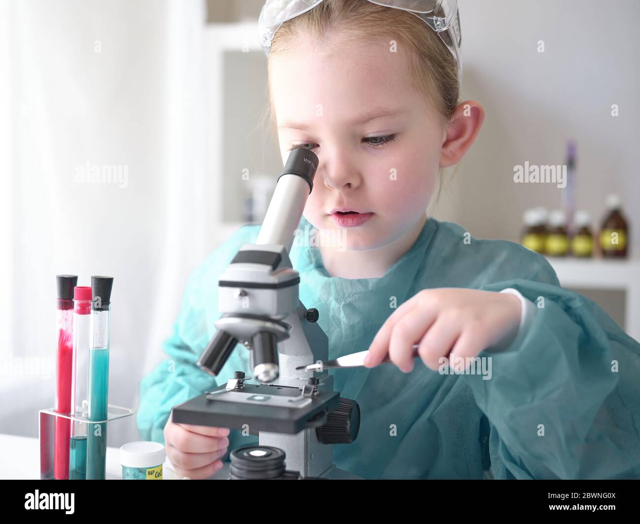 Cute little girl looking into microscope at his desk at home. Young ...