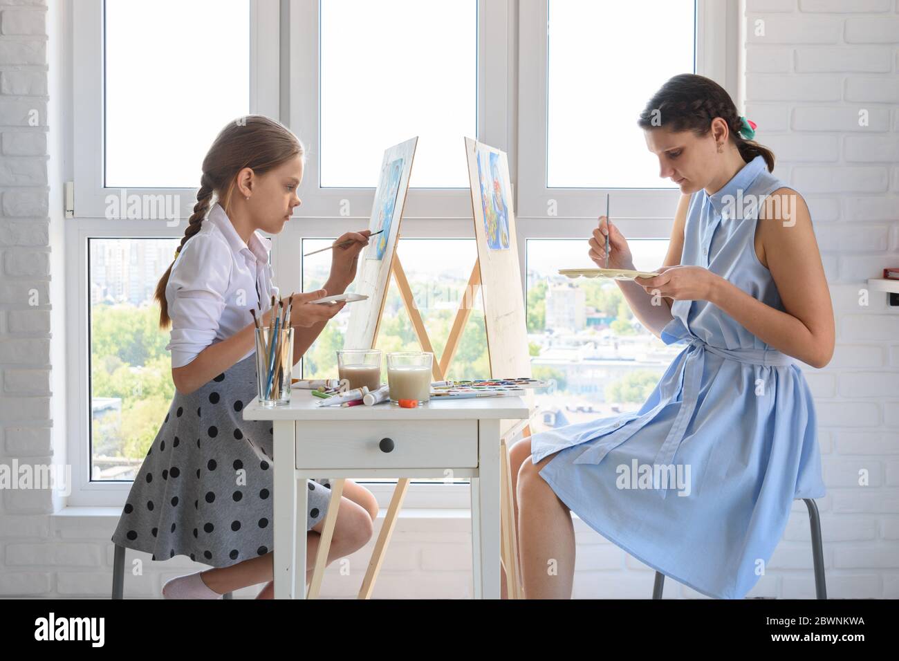 The girl learns to paint at the tutor, together they draw at the window ...