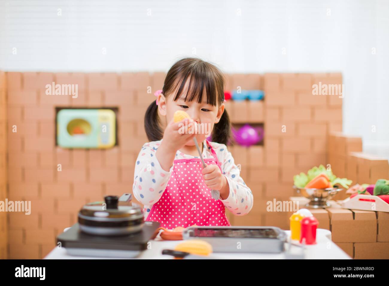 toddler girl pretend play food preparing role against cardboard blocks ...