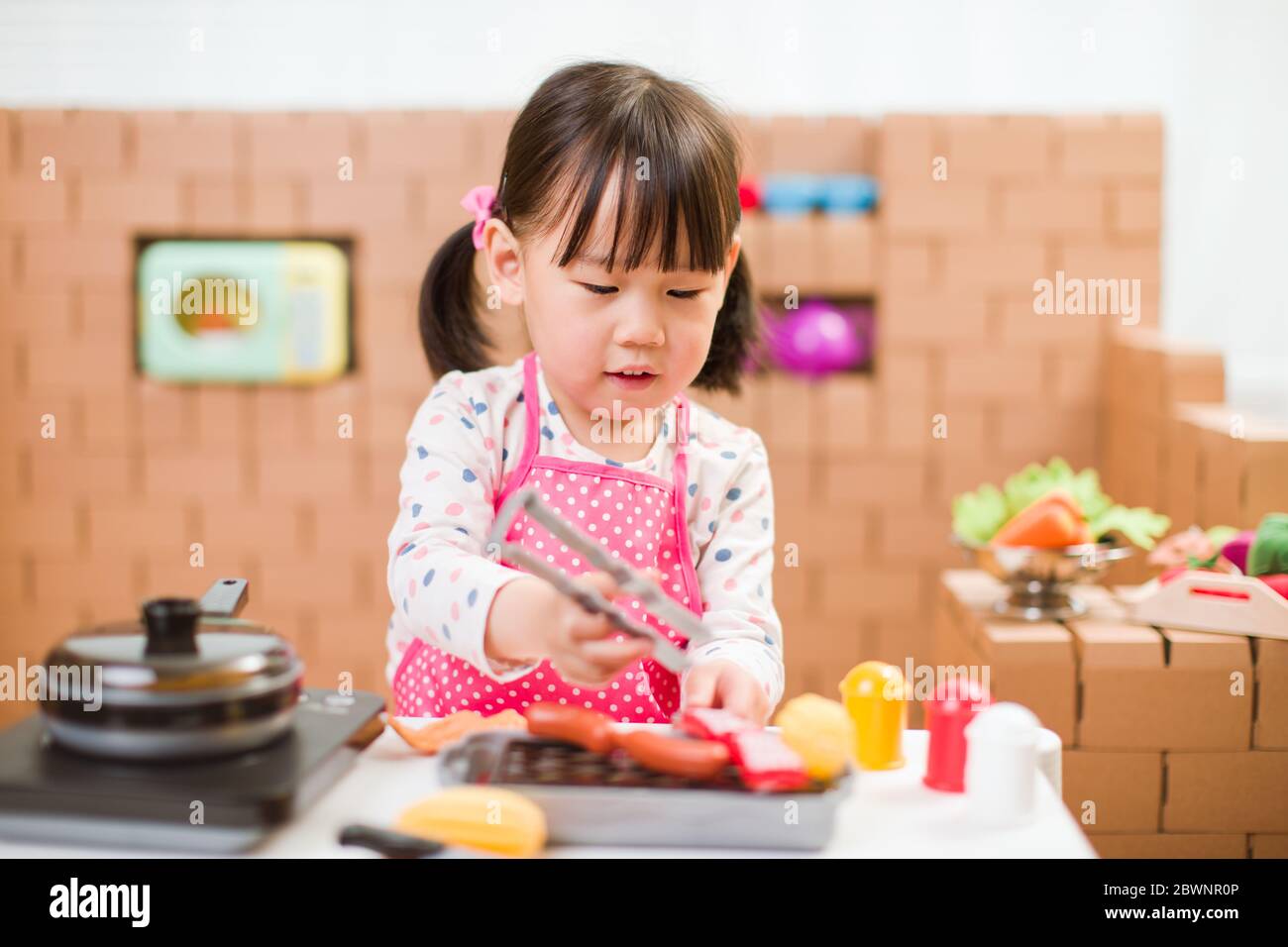 toddler girl pretend play food preparing role against cardboard blocks ...