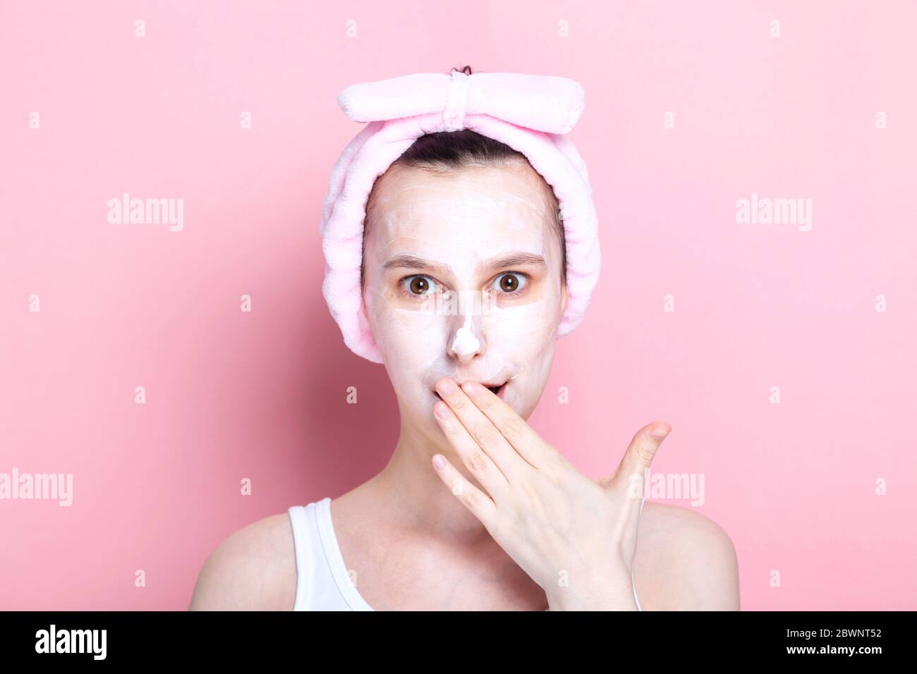 Woman with cosmetic mask on face is surprised to open mouth and cover ...