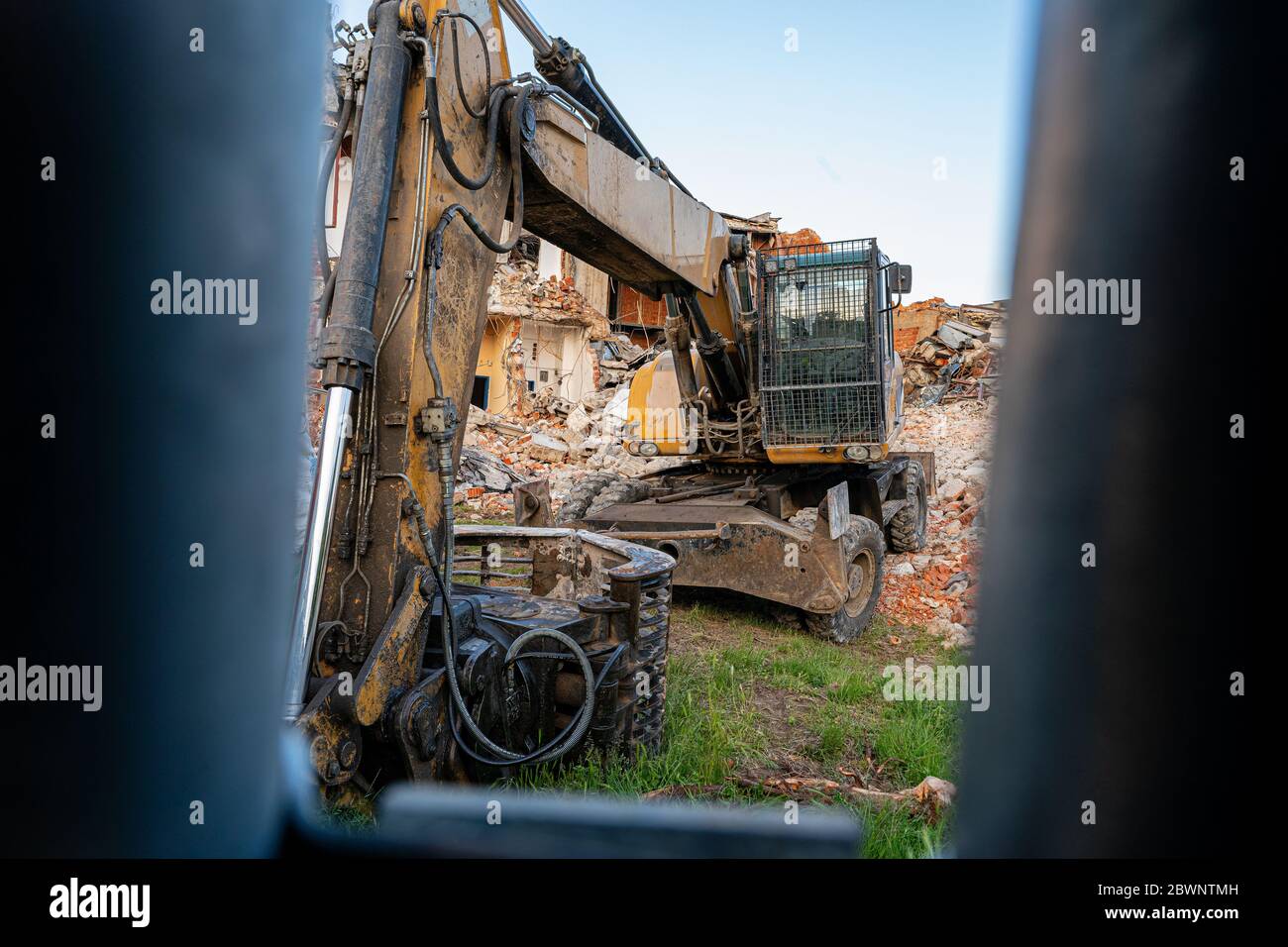 Excavator in the construction yard with ruins behind. Shot through the ...