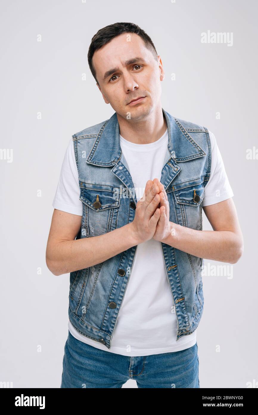 Portrait of beseeching man in denim clothes holding hands in prayer and ...