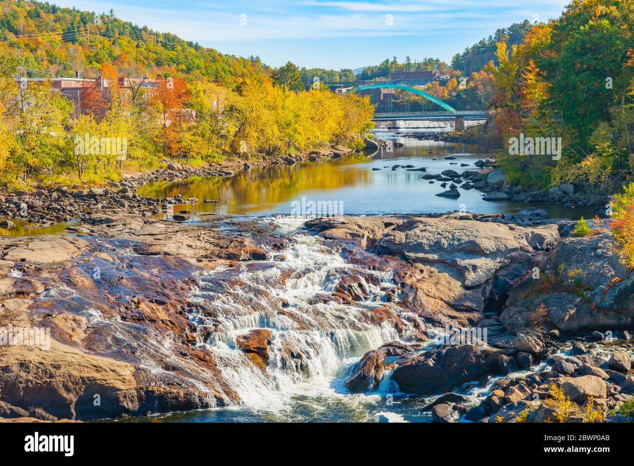 Idyllic stream with bridge and Rumford Falls surrounded by beautiful ...