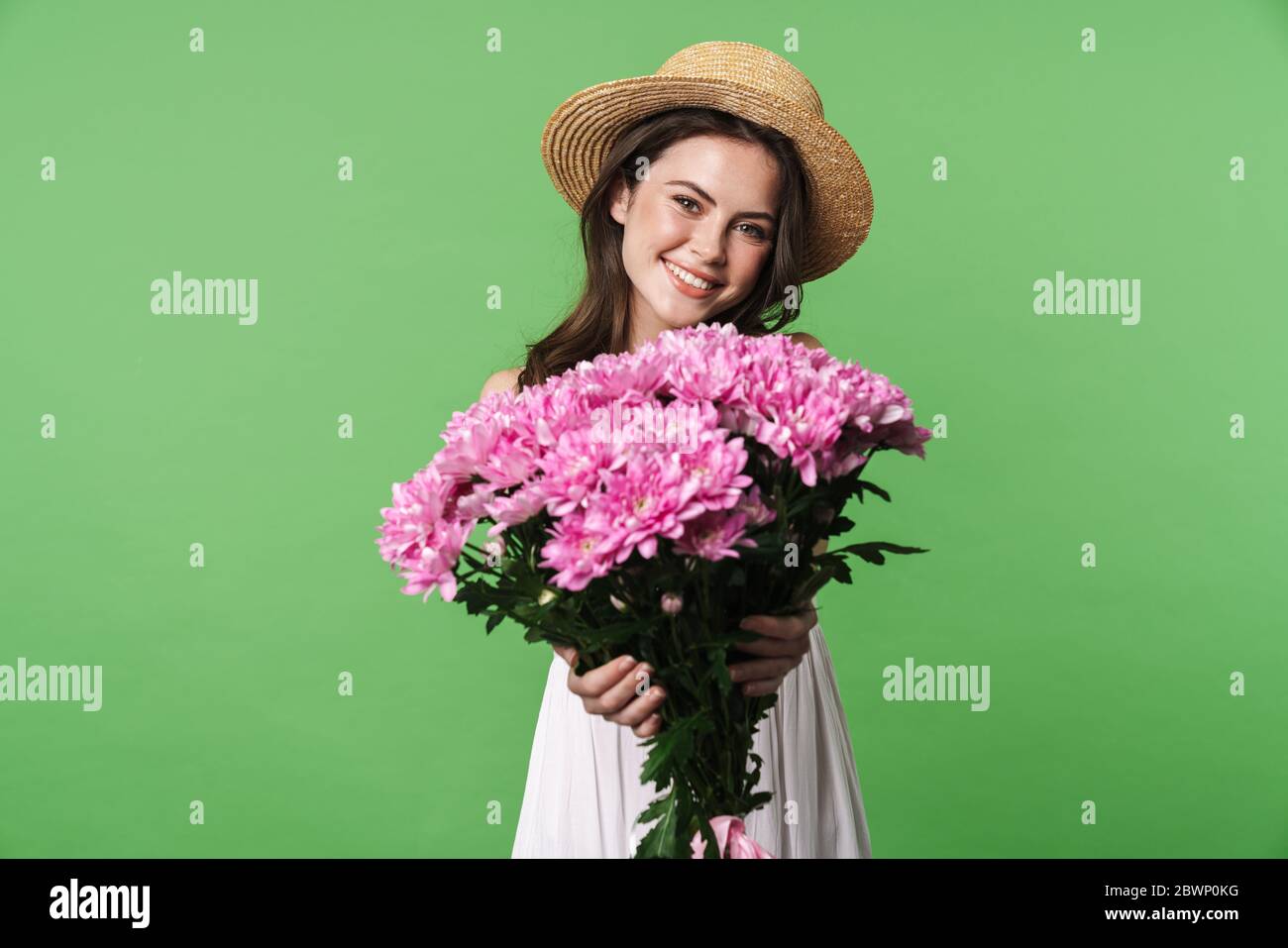 Image of cheerful pretty woman in straw hat smiling and holding flowers ...