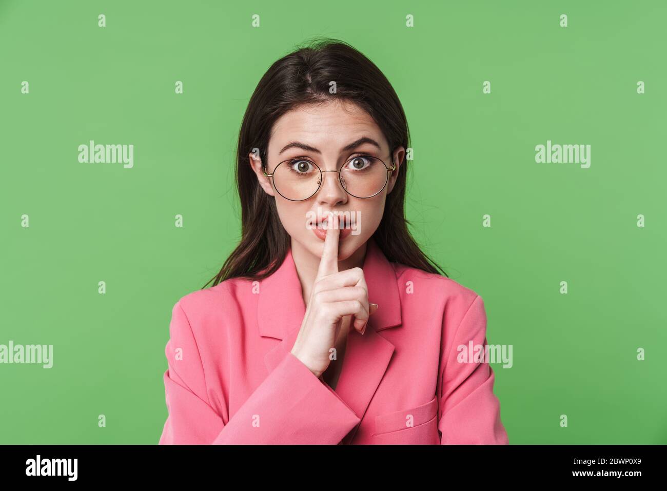 Image of excited young woman in eyeglasses making silence gesture ...