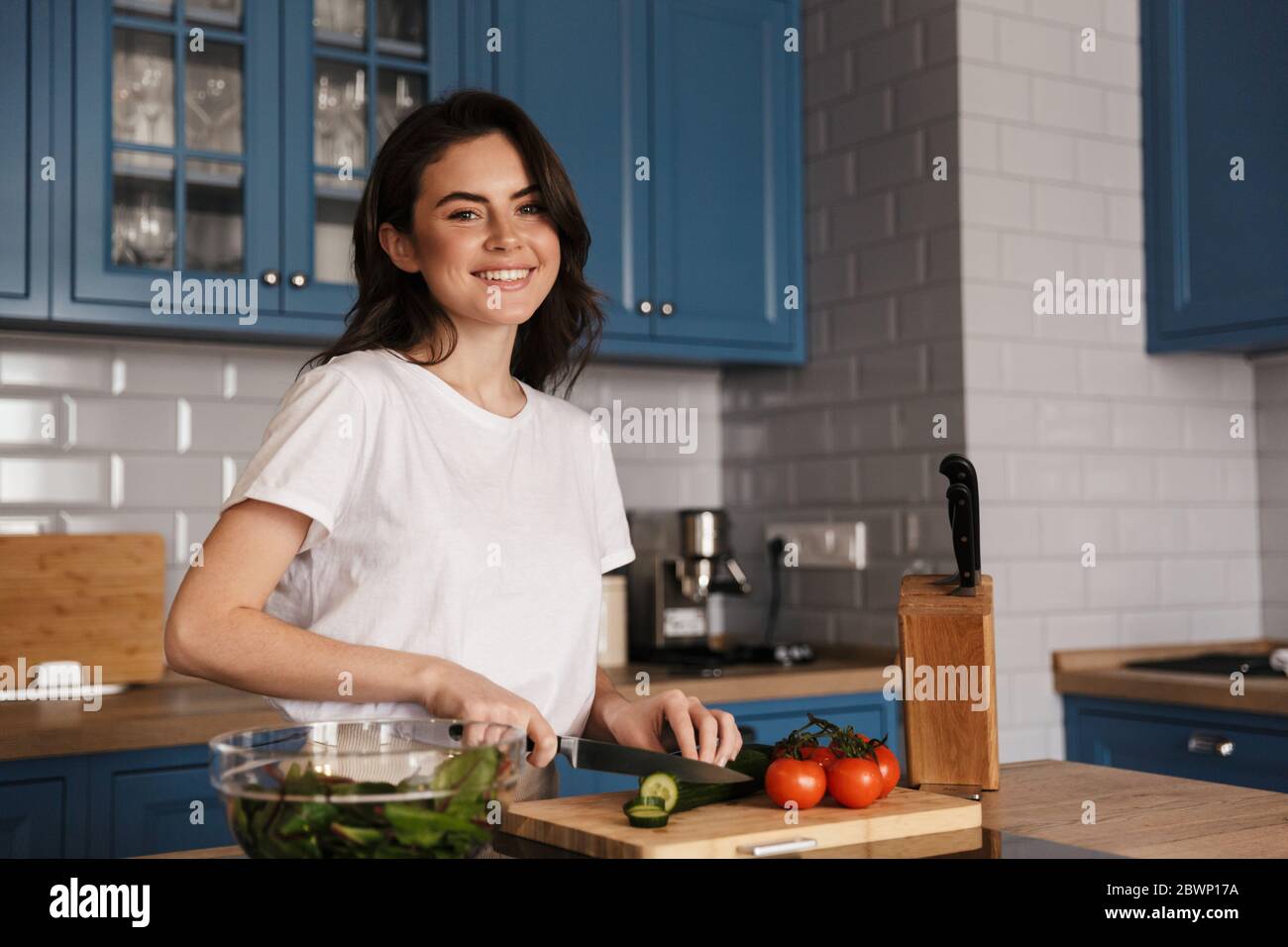 Beautiful young brunette woman cooking salad while standing at the ...