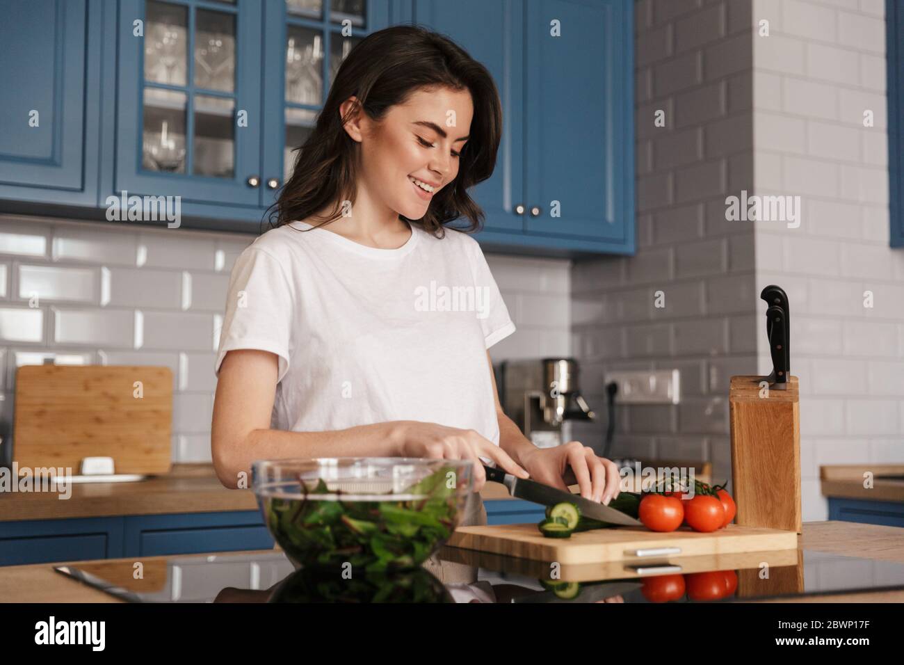Beautiful young brunette woman cooking salad while standing at the ...