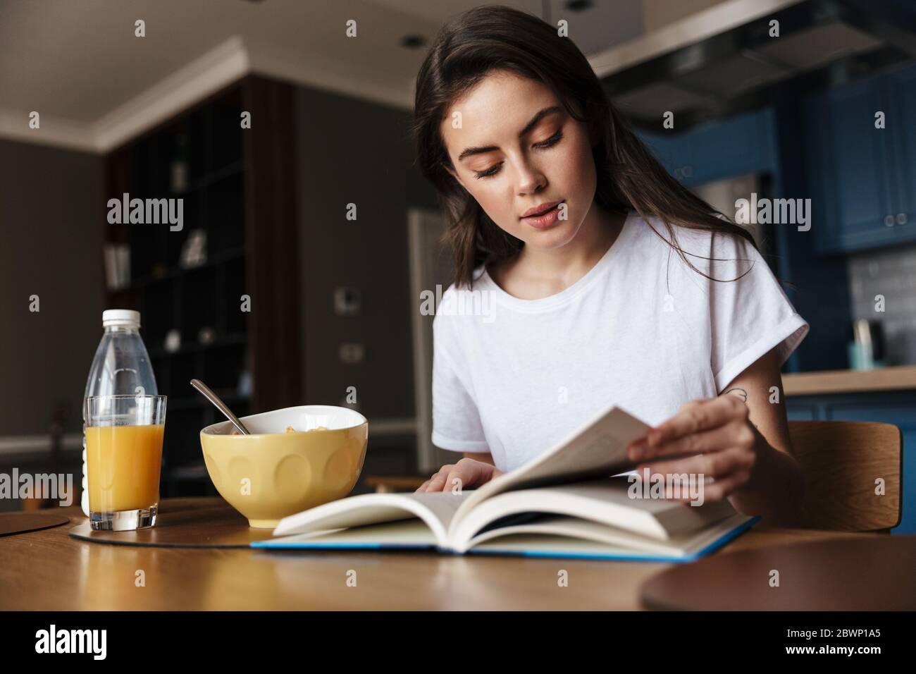 Attractive young brunette woman having a healthy breakfast reading a ...