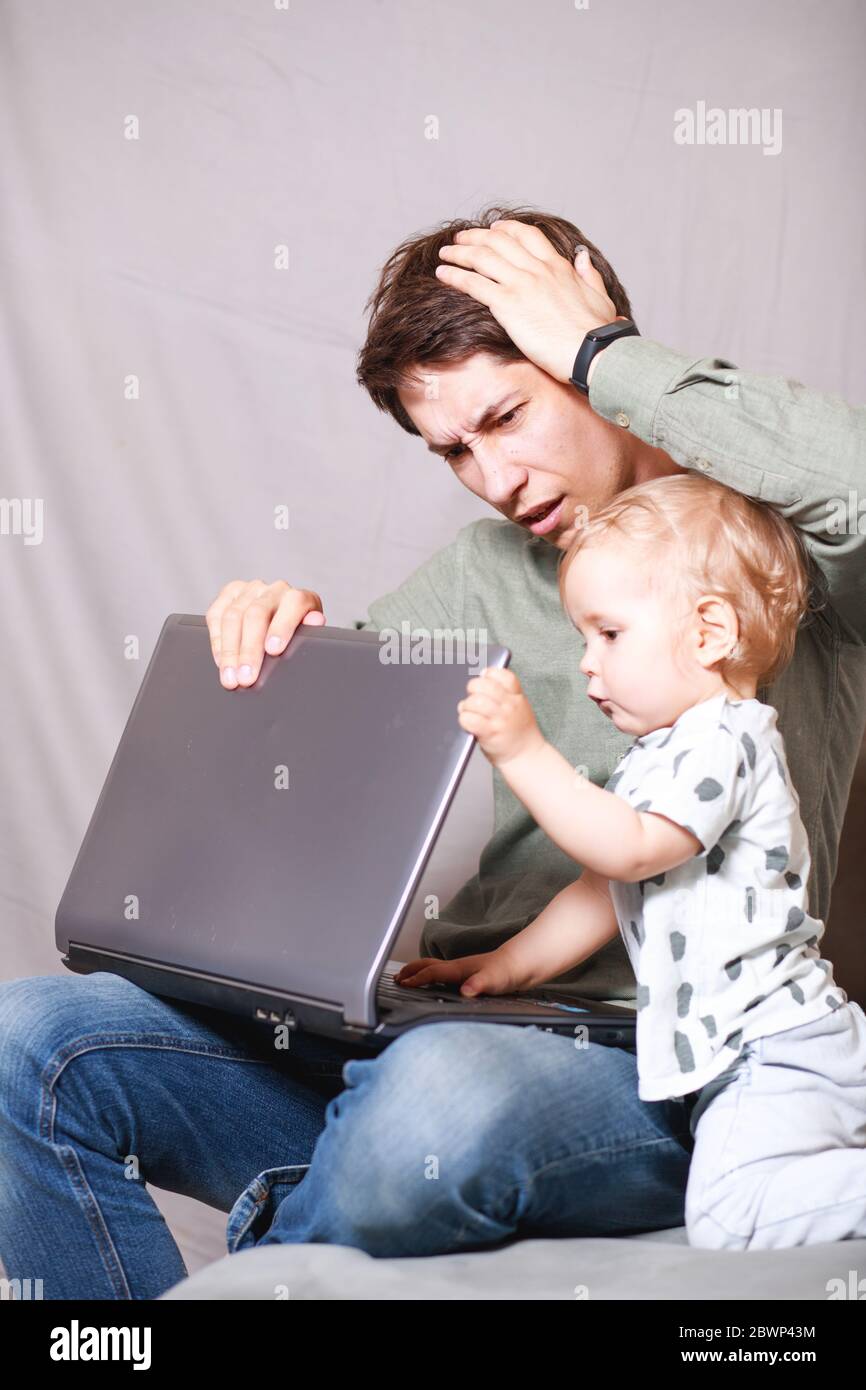 Handsome young man working at home with a laptop with a baby on his ...