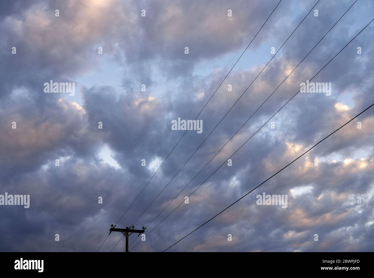 Utility pole and overhead power supply lines against the sky and clouds ...