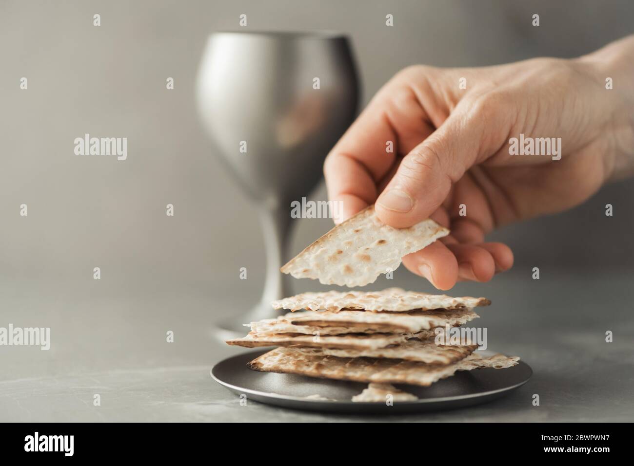Hands with chalice and communion matzo bread, wooden cross on grey ...