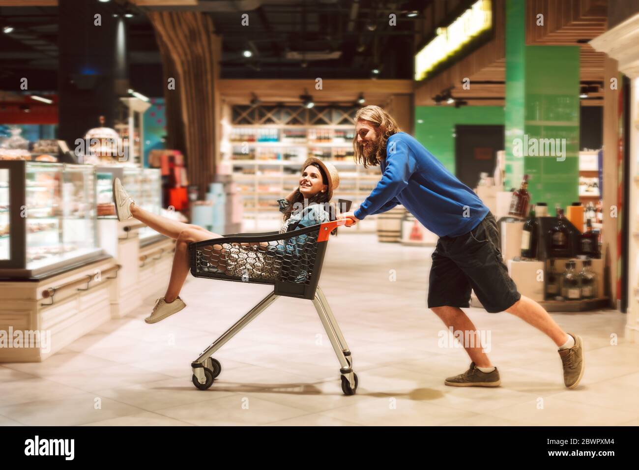 Young guy pushing shopping trolley with pretty girl inside while ...