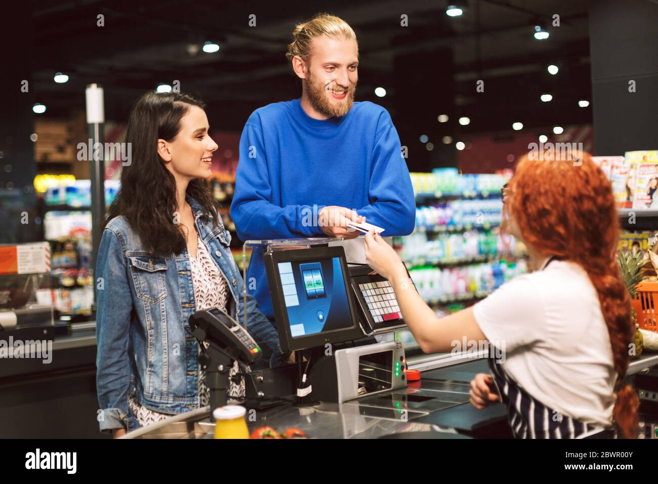Young cheerful couple standing near cashier desk while happily giving ...
