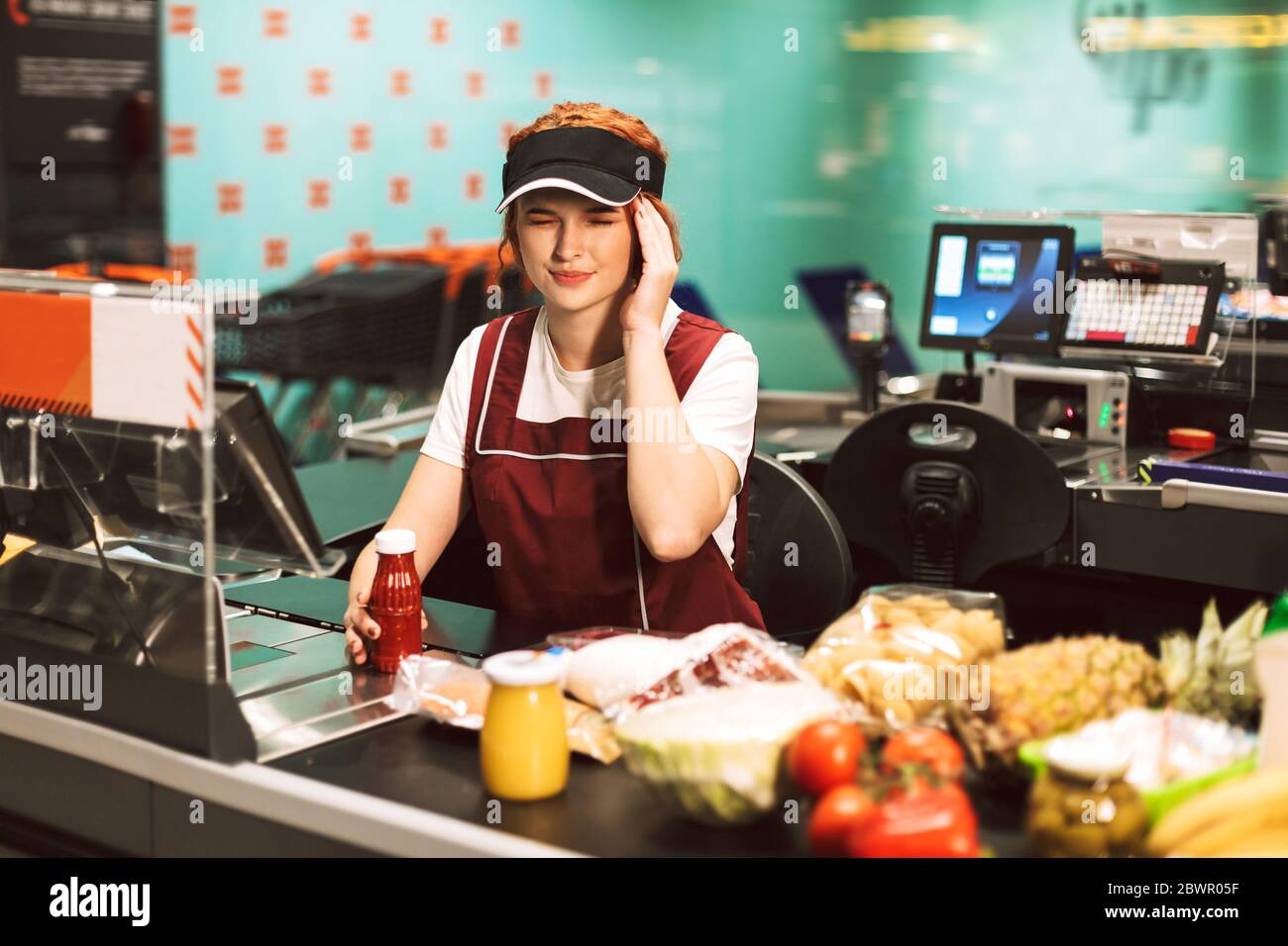 Young female cashier in uniform with headache working in supermarket Stock Photo - Alamy