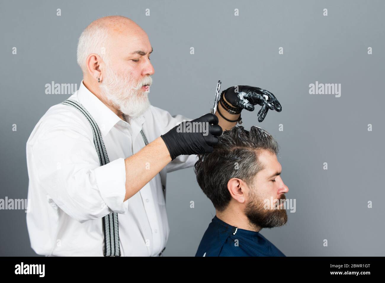 Hair salon. Coloring. Bearded man in process of hair coloring. Applying ...