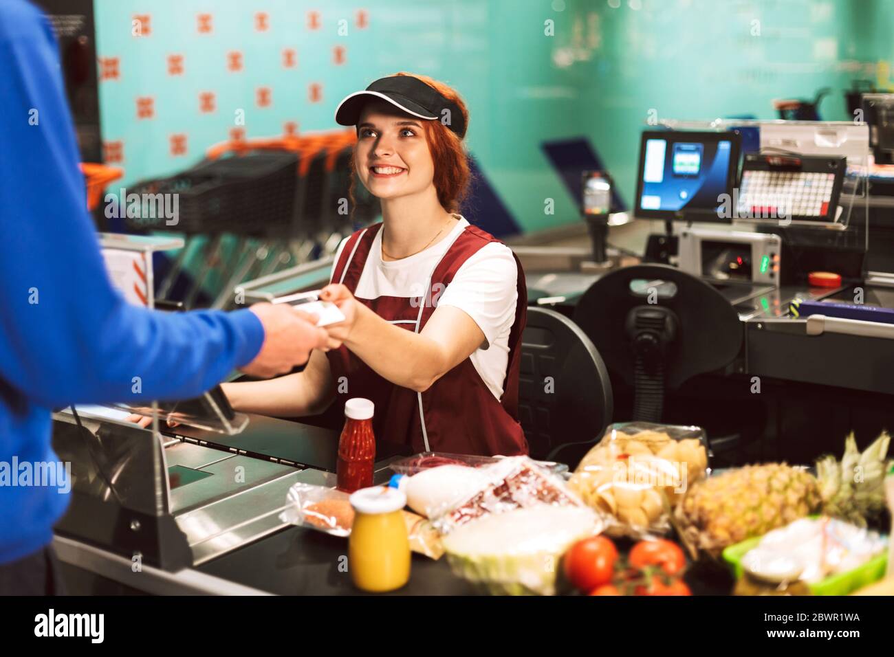 Beautiful smiling female cashier in uniform happily looking at ...