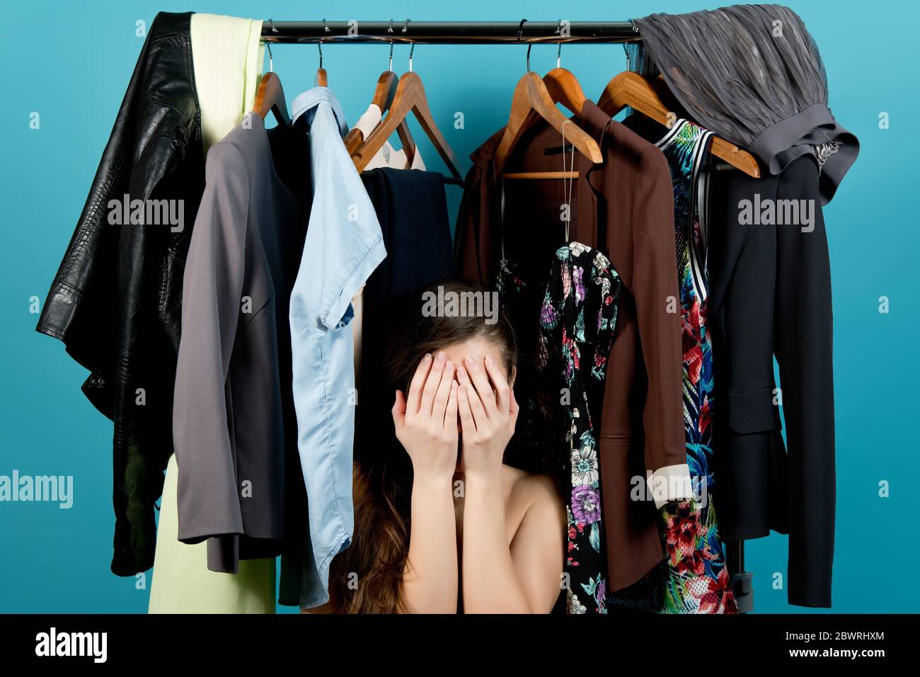 Girl covers her face, lost in the choice of clothes on the background ...