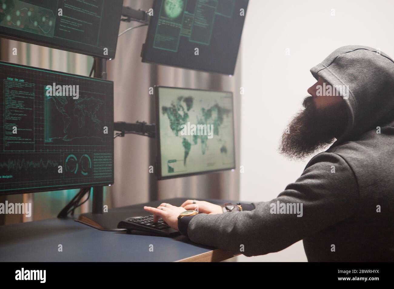 Side view of bearded male hacker wearing a hoodie launching a cyber ...