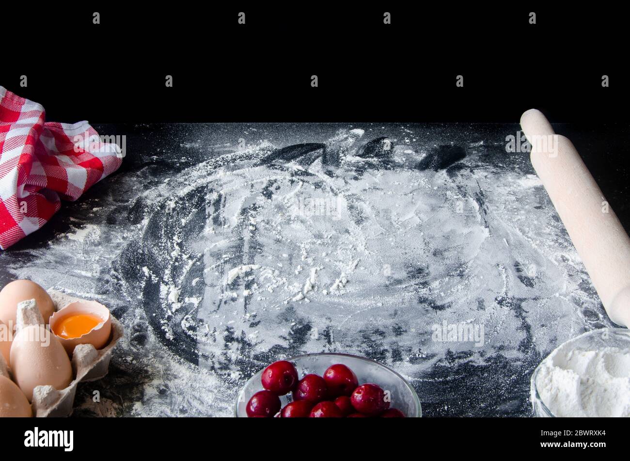 Flour and ingredients for sweet berry pie lie on the black table Stock ...