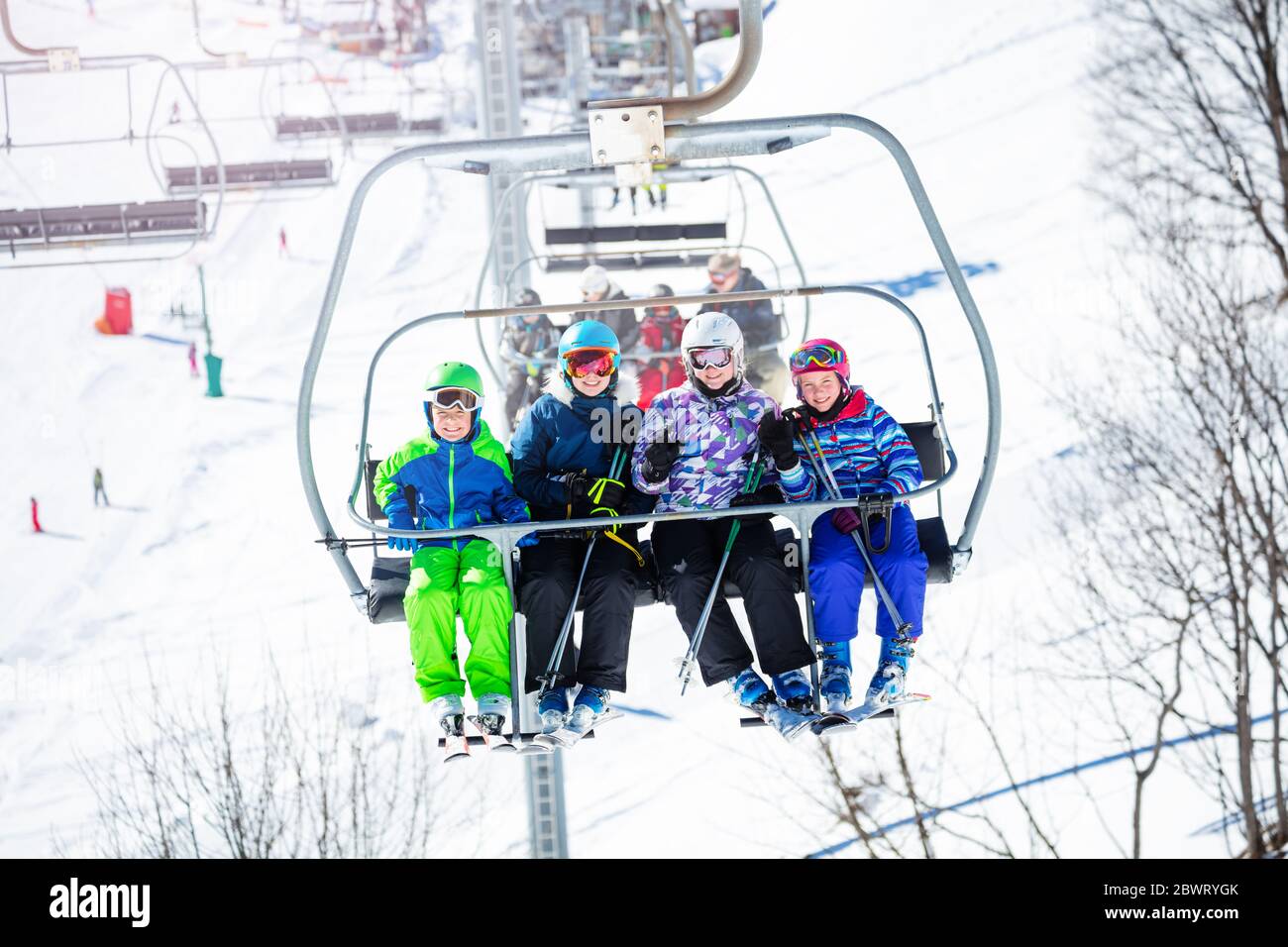 Group of four children sit on the chair lift going to the mountain top ...