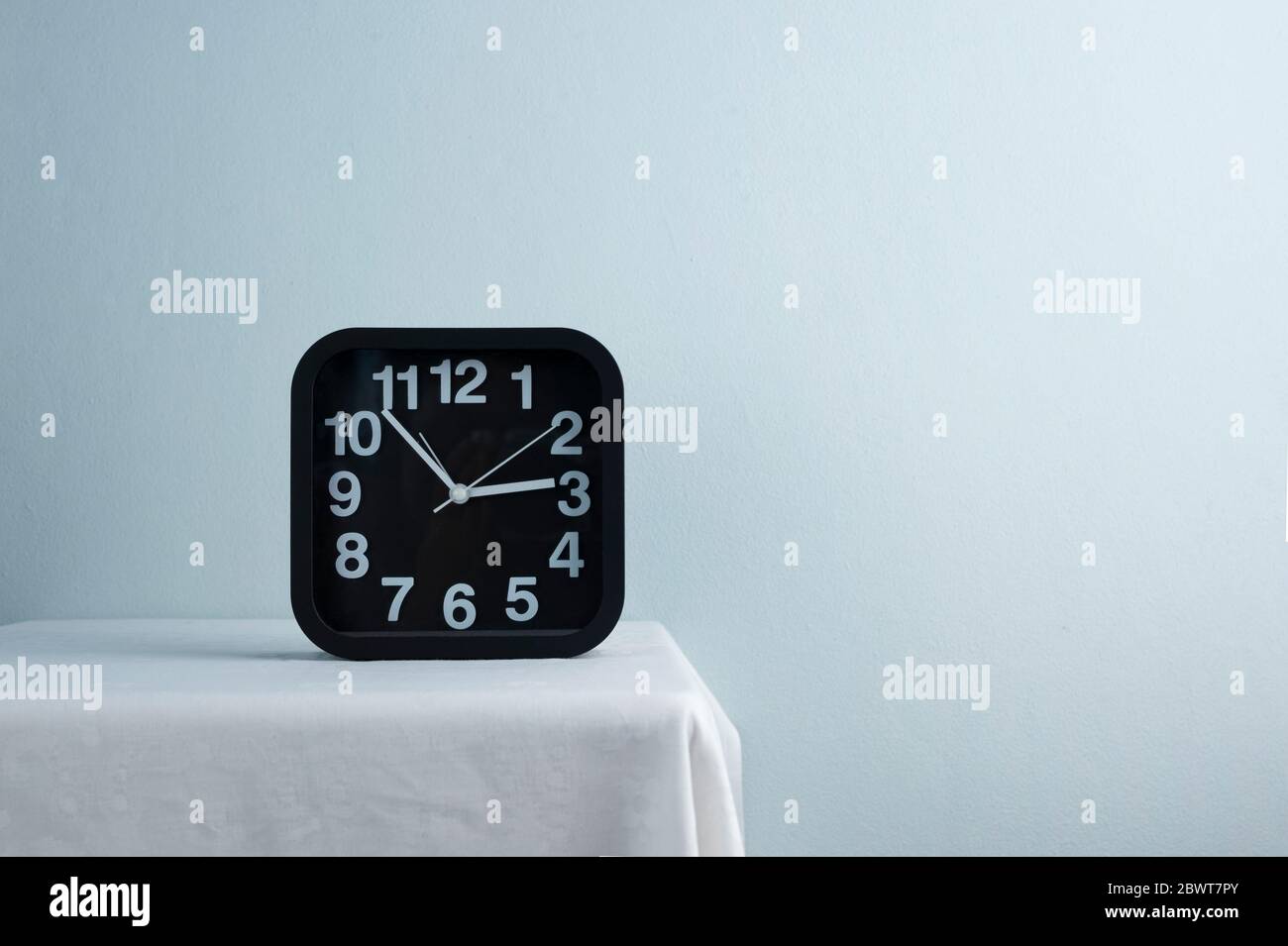black and white modern clock at three pm on table in light blue ...