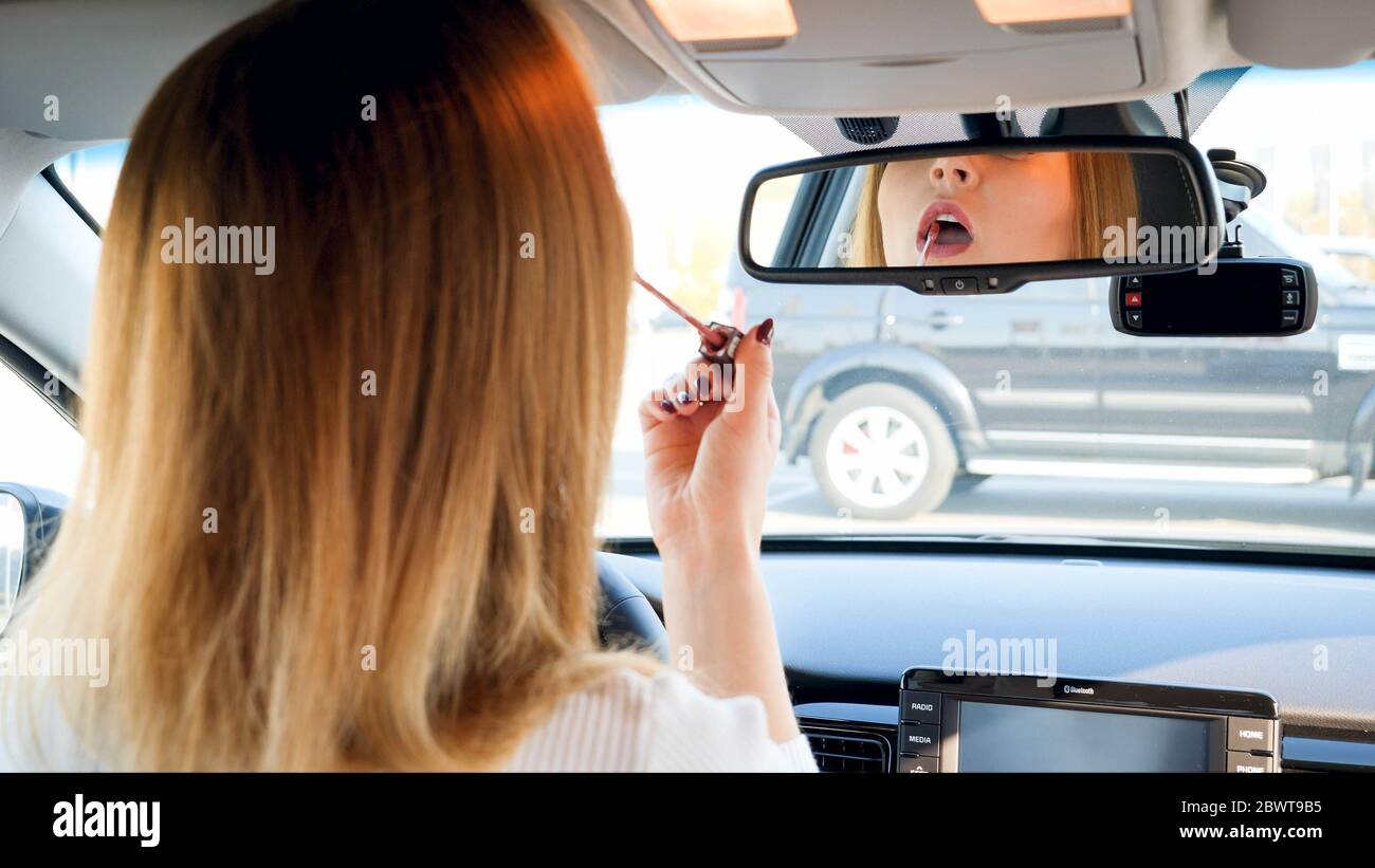 Portrait of beautiful young woman looking in car mirror while painting ...