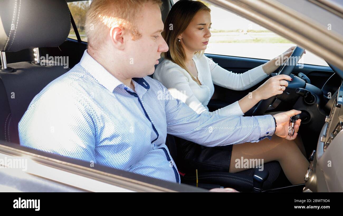 Portrait of male driving instructor teaching young woman how to power ...