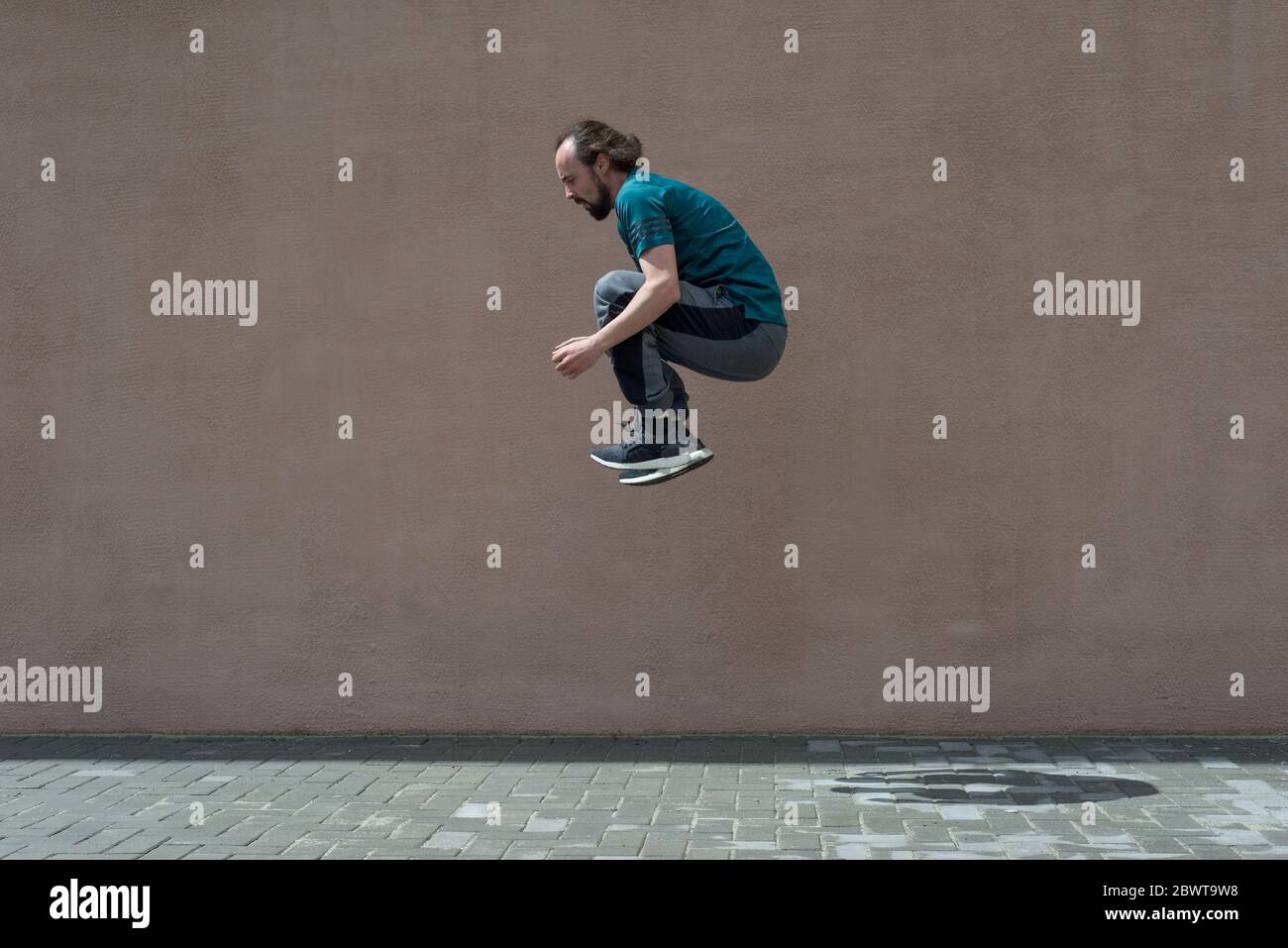 young bearded guy sortsman jumping on the background of a pink street ...