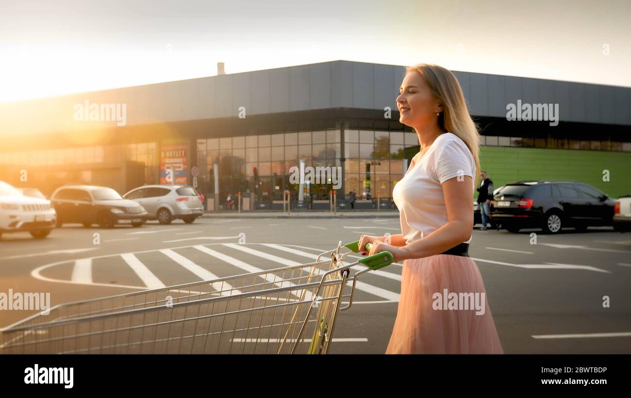 Beautiful smiling blonde girl pushing shopping cart while walking on ...