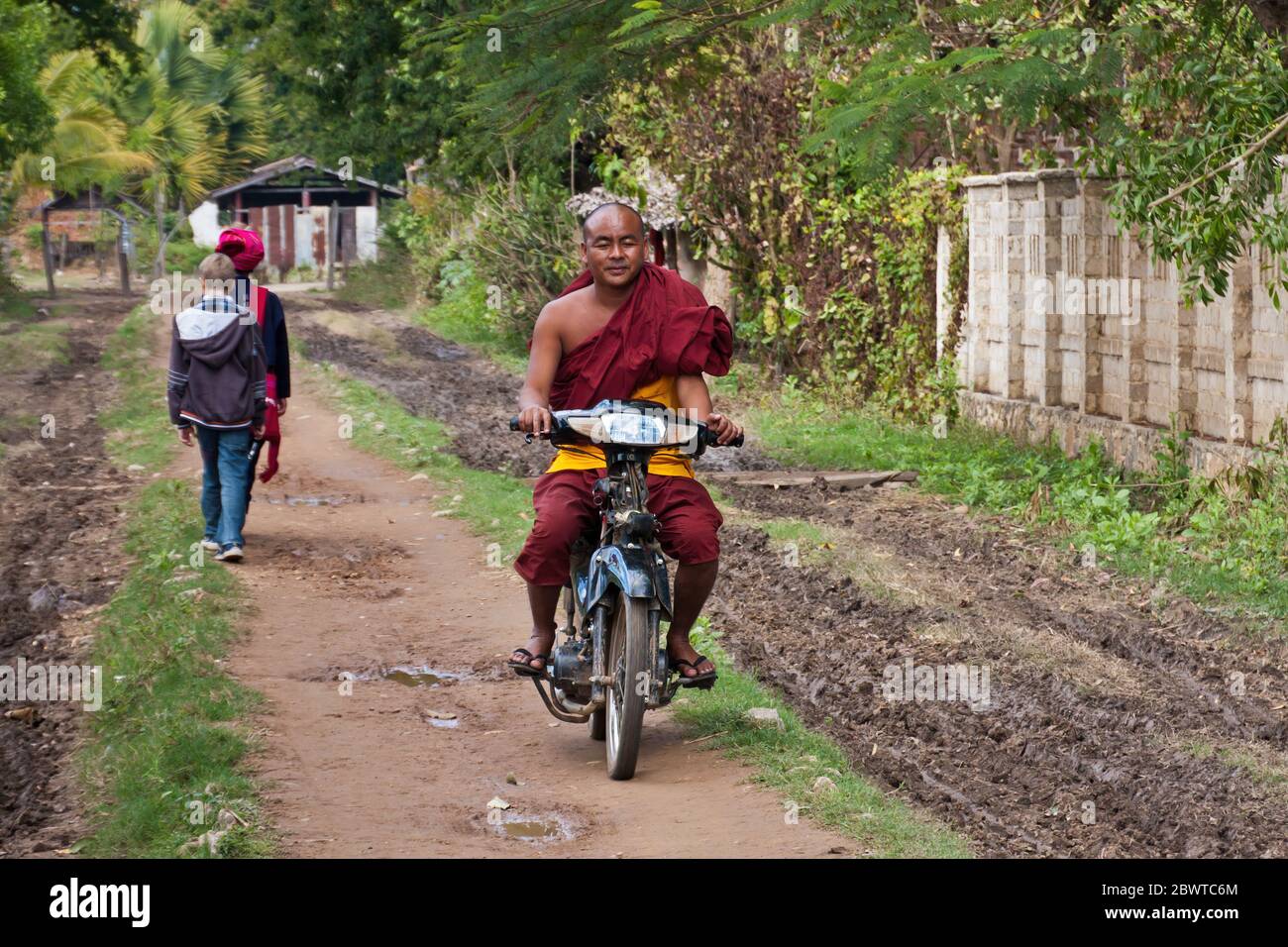 A happy Buddhist monk driving a motorbike on a village street in Samka ...