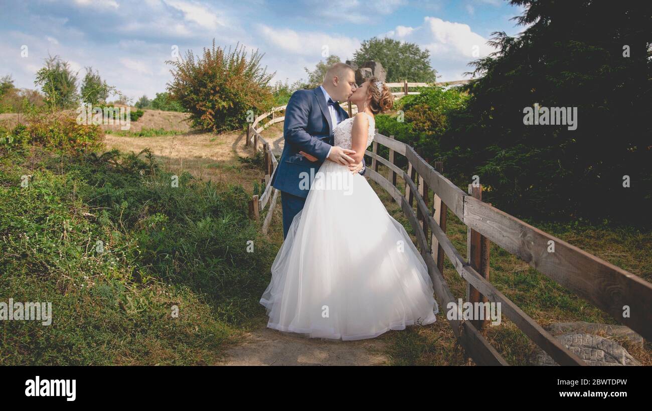 Toned photo of beautiful newly married couple kissing at long wooden ...
