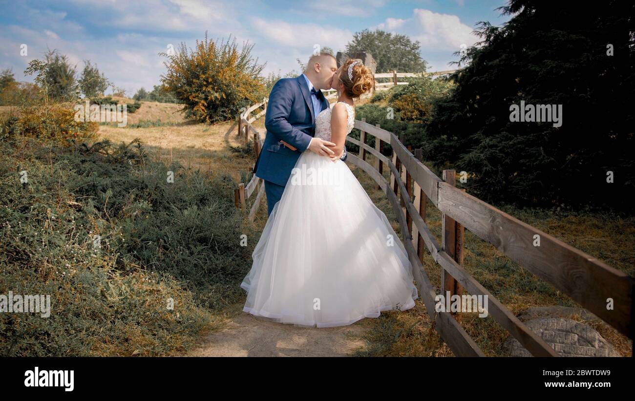 Toned image of newly married bride and groom kissing at long wooden ...