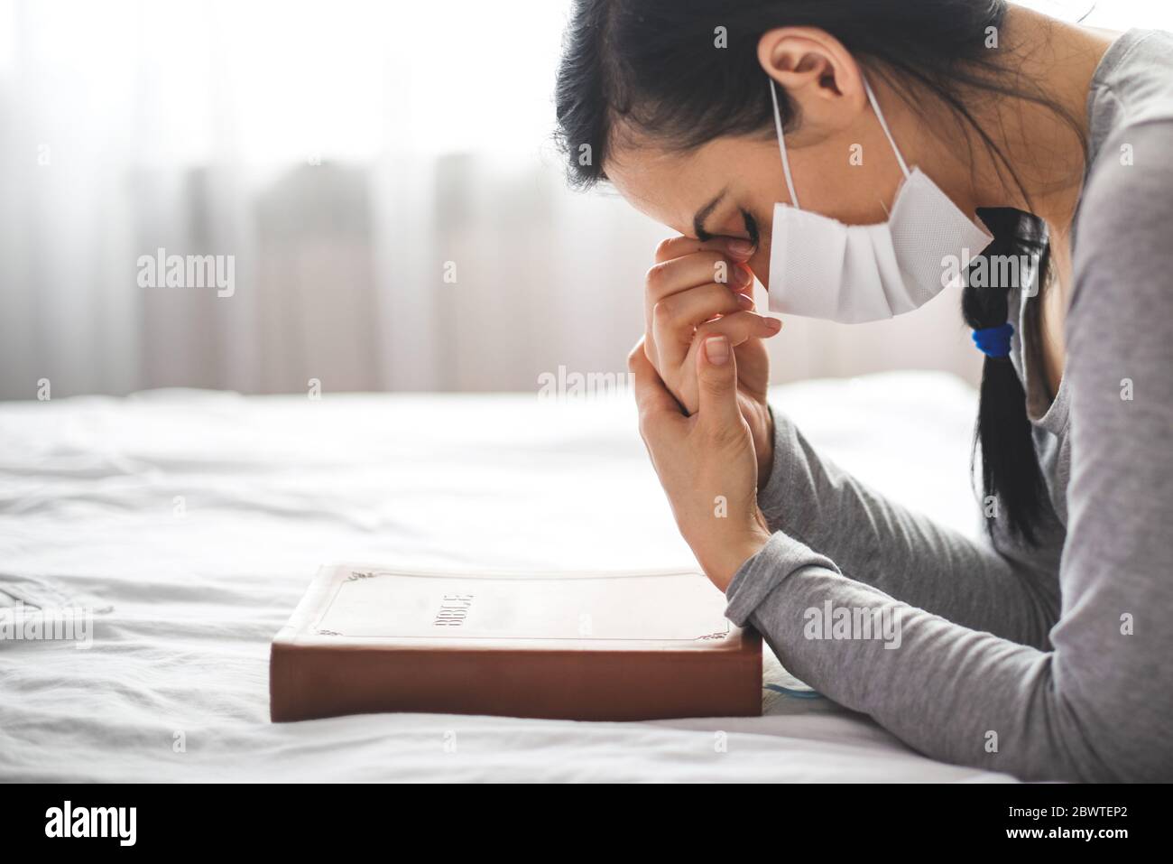 Woman with mask praying next to bed with her bible near Stock Photo - Alamy