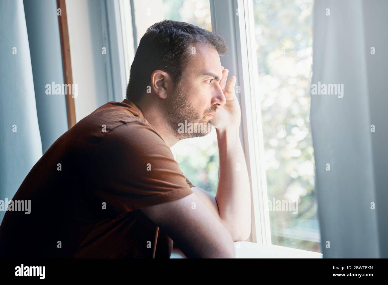 Portrait of one guy feeling sad and looking through window Stock Photo ...