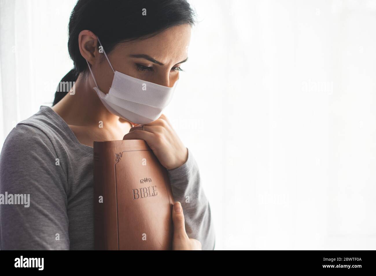 Portrait of a woman with a surgical mask on her face and a bible held ...