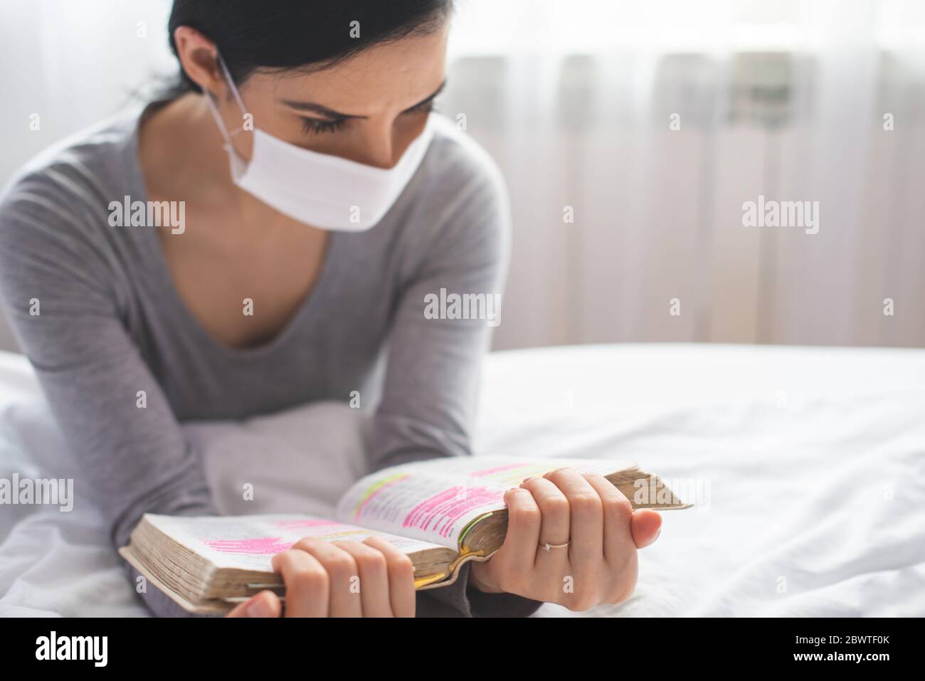 Quarantined woman with mask reading from bible and praying Stock Photo ...
