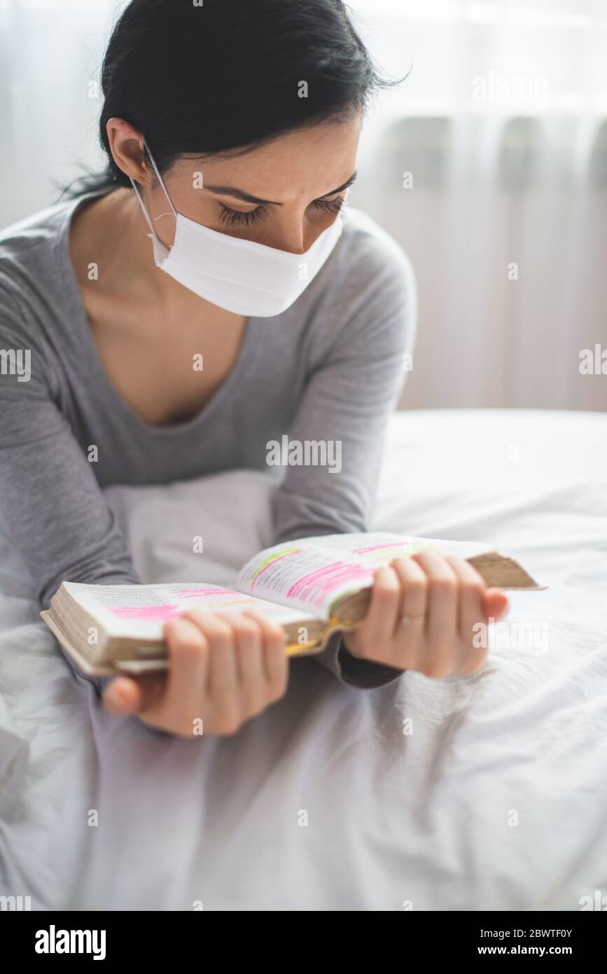 Quarantined woman with mask reading from bible and praying Stock Photo ...