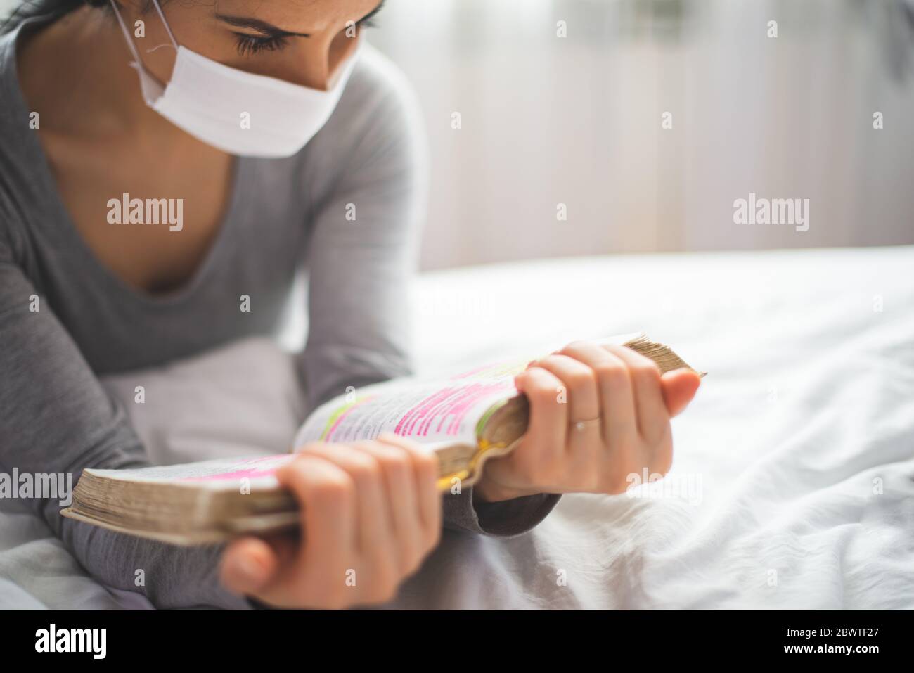 Quarantined woman with mask reading from bible and praying Stock Photo ...