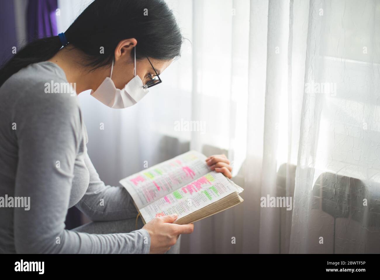 Quarantined woman with mask reading from bible and praying Stock Photo ...