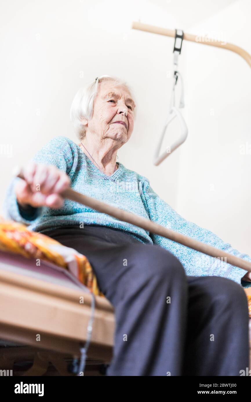 Elderly 96 years old woman exercising with a stick sitting on her bad ...